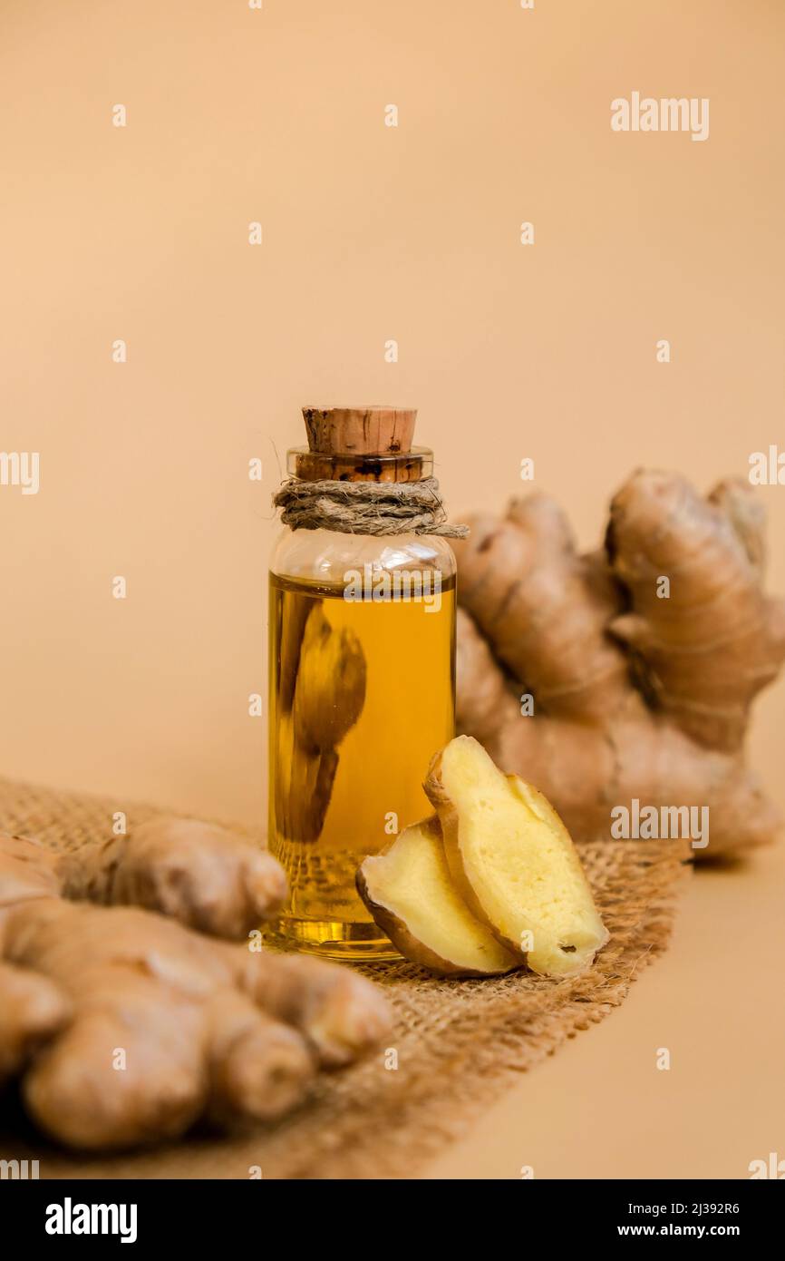 Glass bottle of essential ginger oil, ginger root on beige background ...