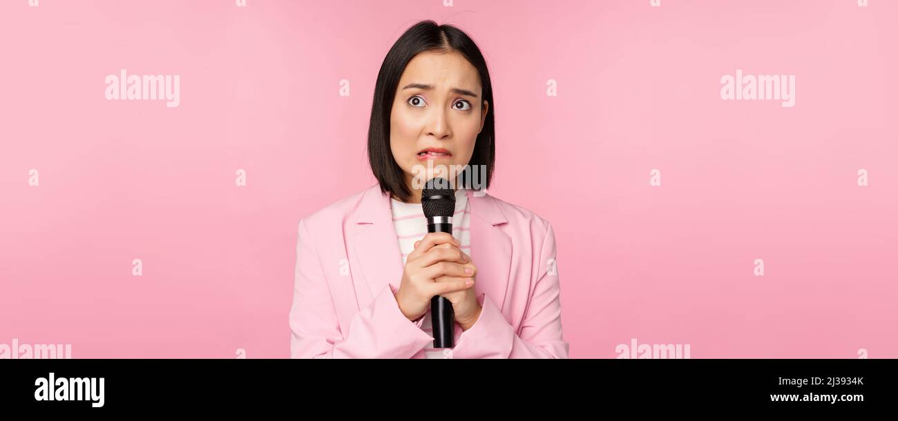 Anxious asian lady in suit, talking in public, giving speech with ...