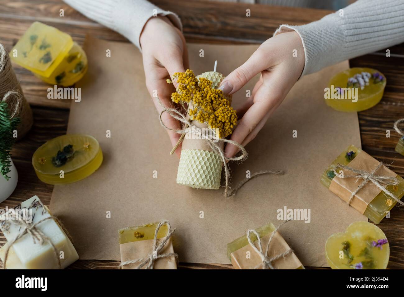 Top view of craftswoman holding handmade candle with flower near soap ...