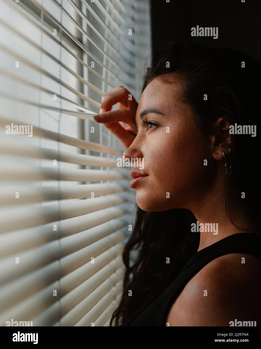 A Caucasian girl looking through window blinds at home Stock Photo - Alamy