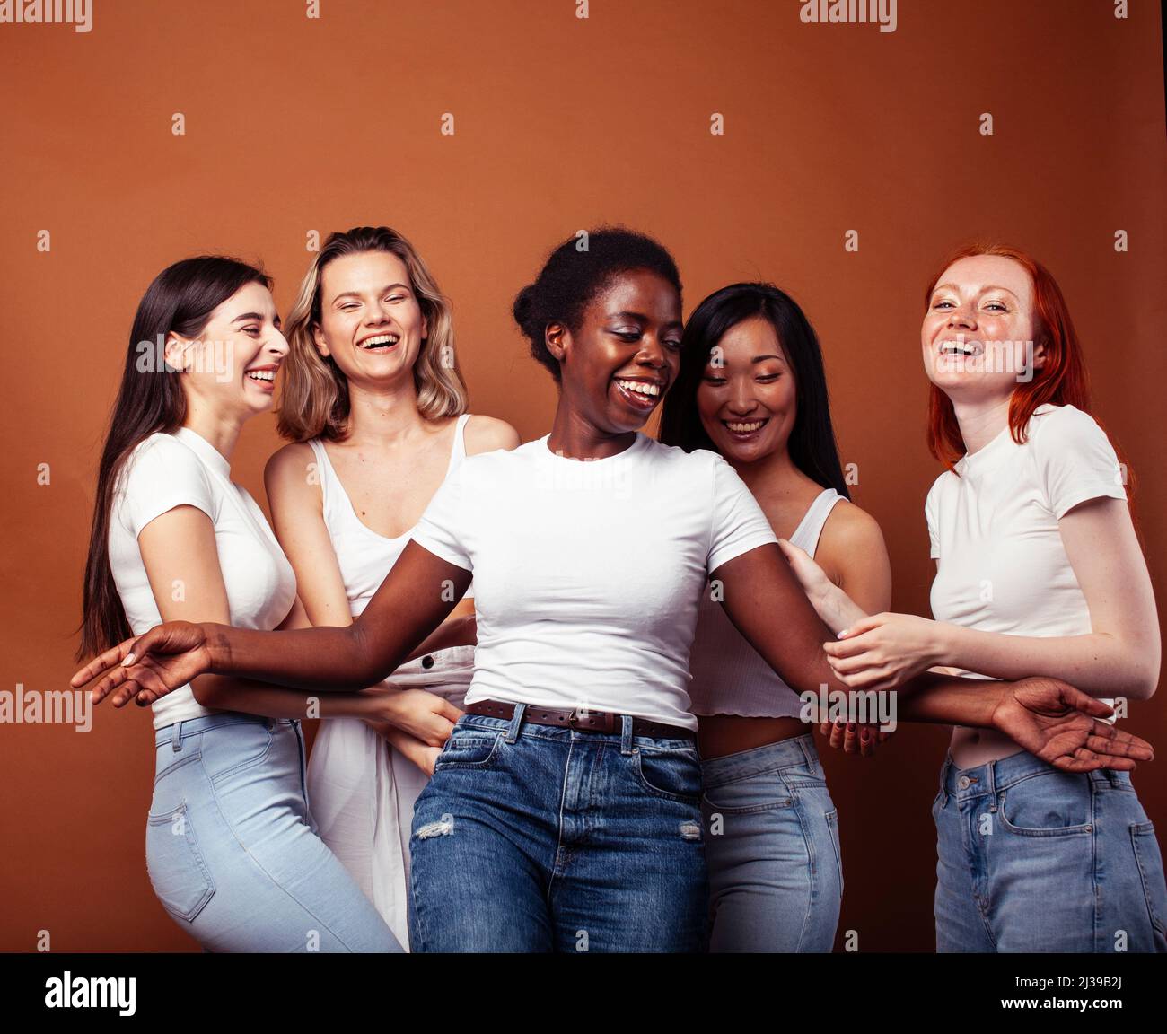 young pretty asian, caucasian, african woman posing cheerful together on brown background ...