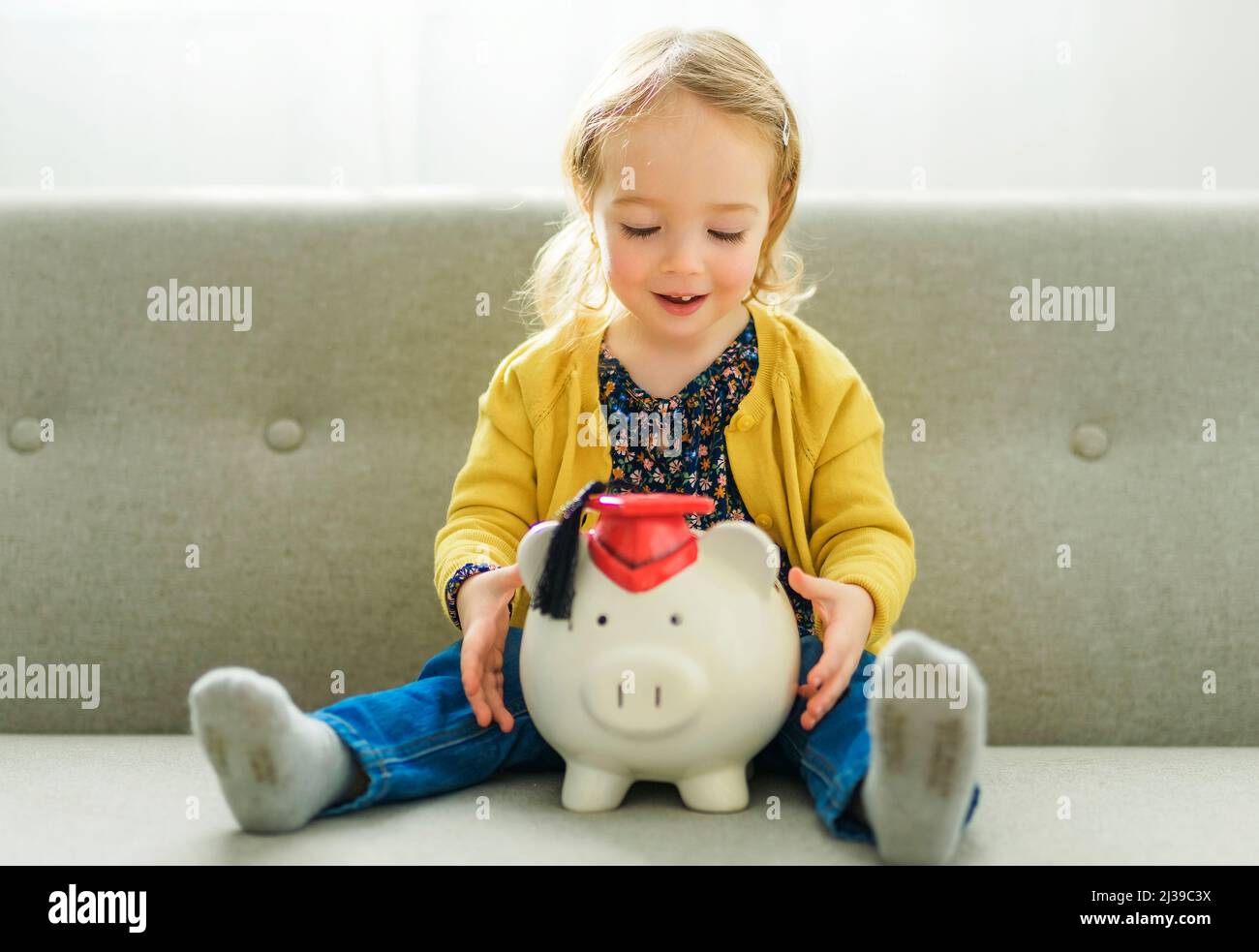 Cute little baby girl putting a coin into a pink piggybank seated on a ...