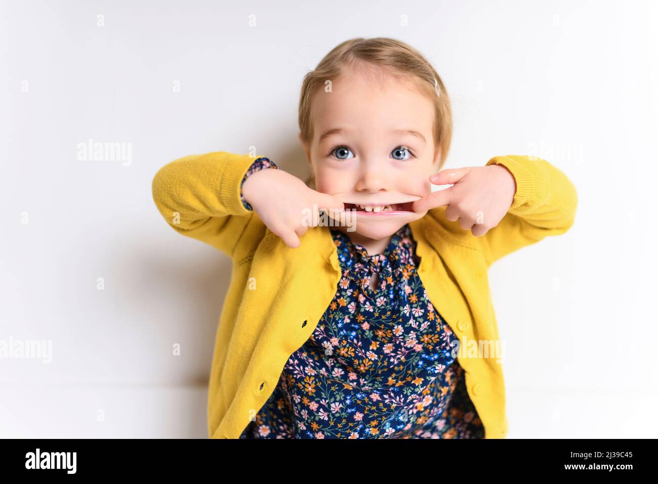 Cute playful baby girl sitting on the floor of a white background doing ...
