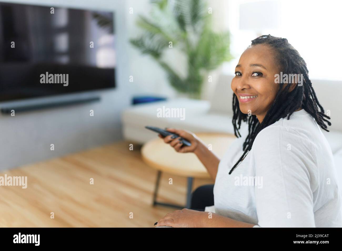 Portrait of an african woman sit on the sofa and holding remote control ...