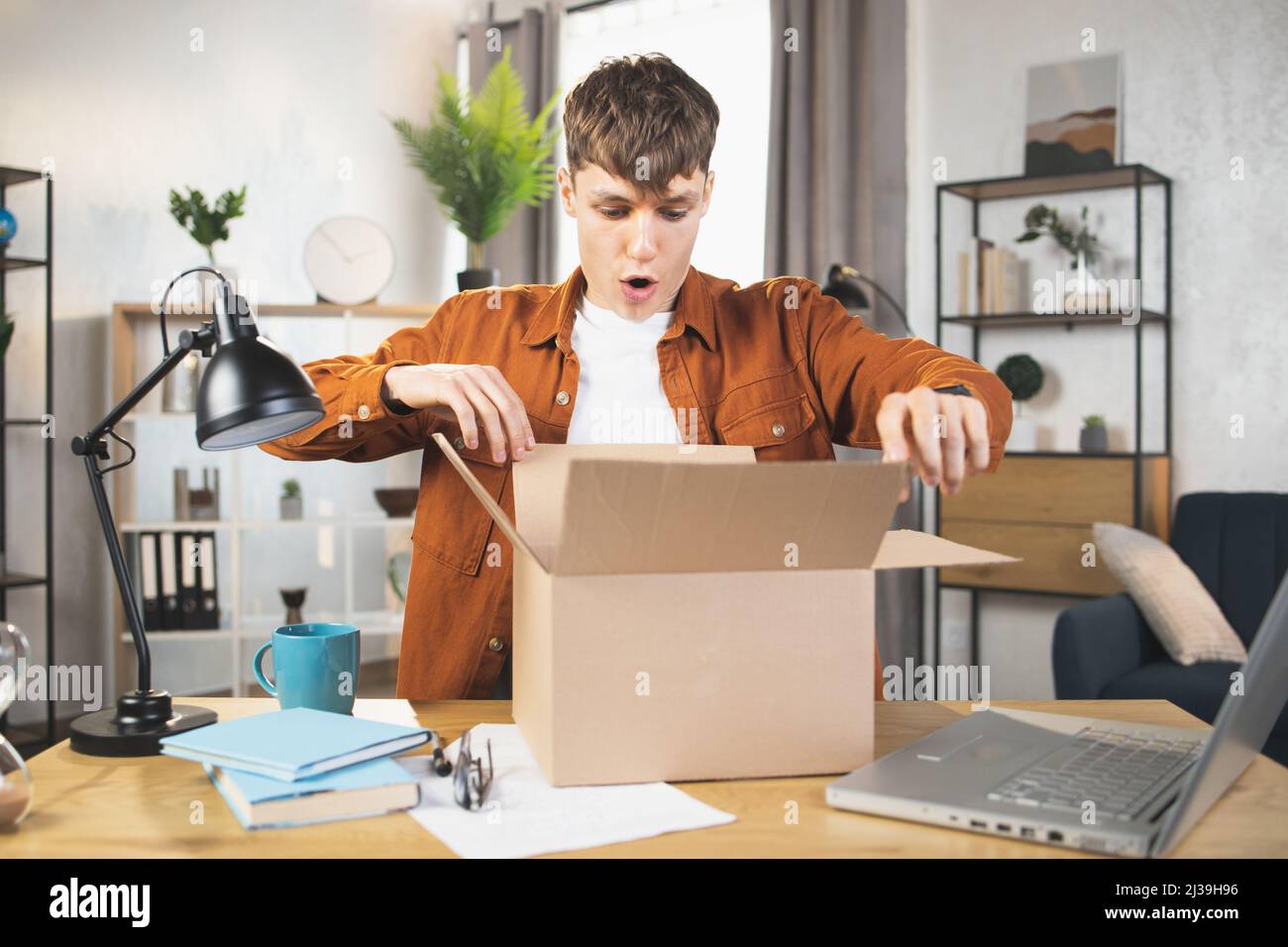 Excited surprised young Caucasian man opening box with ordered goods ...