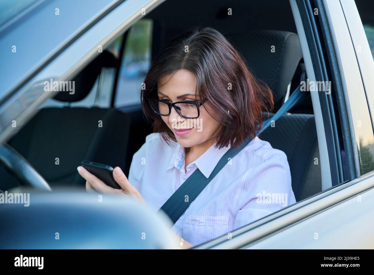 Confident female driver with smartphone driving a car Stock Photo - Alamy