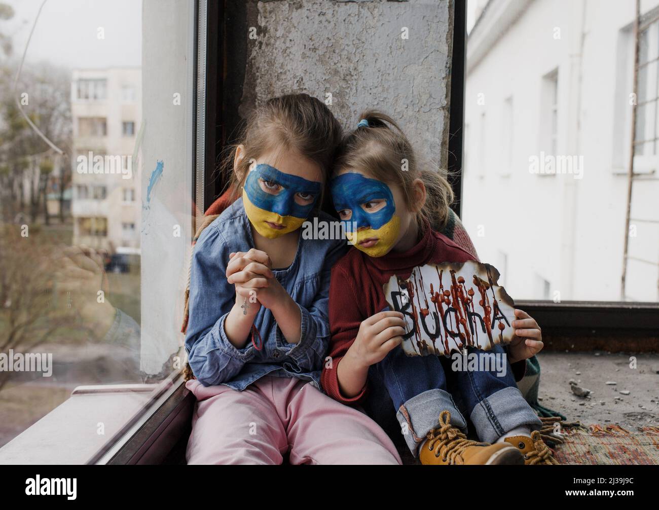 Two little girls with Ukrainian flags painted on their faces are ...