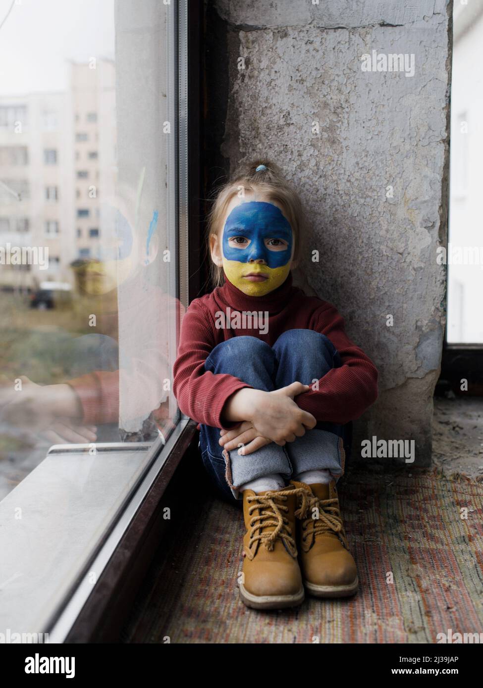 a little girl with a Ukrainian flag painted on her face is sitting ...
