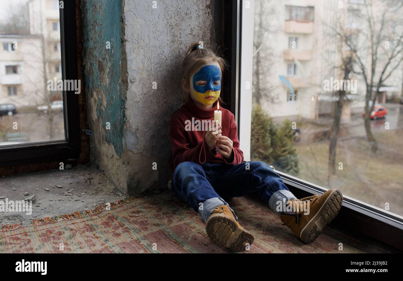 a little girl with a Ukrainian flag painted on her face prays for the ...