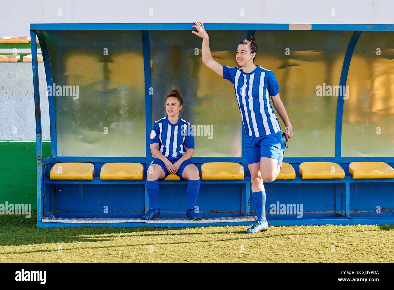 Two women soccer players look out over the soccer field from the bench ...