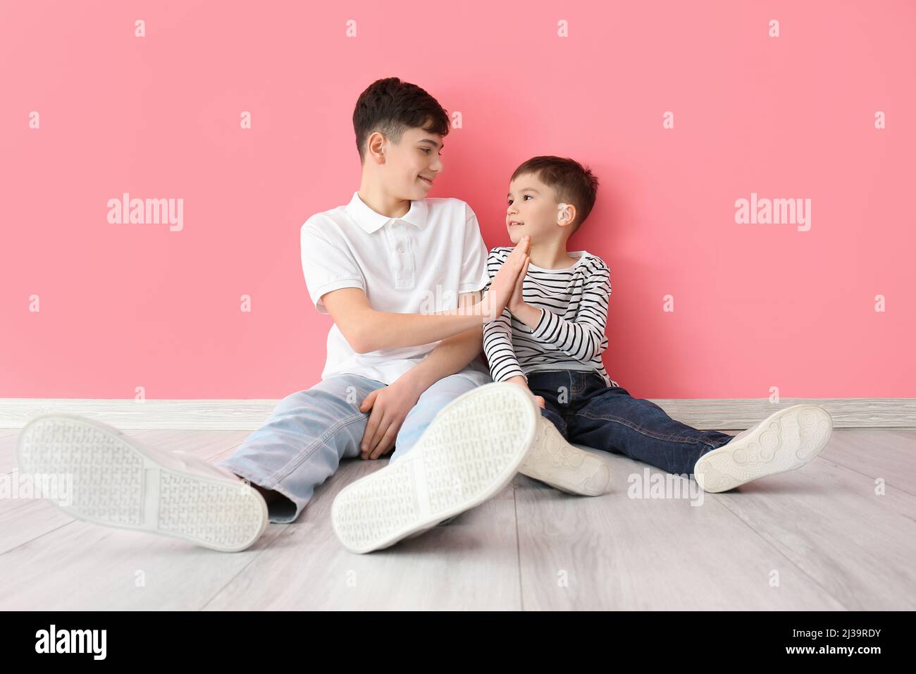 Portrait of cute brothers giving high-five to each other near color ...