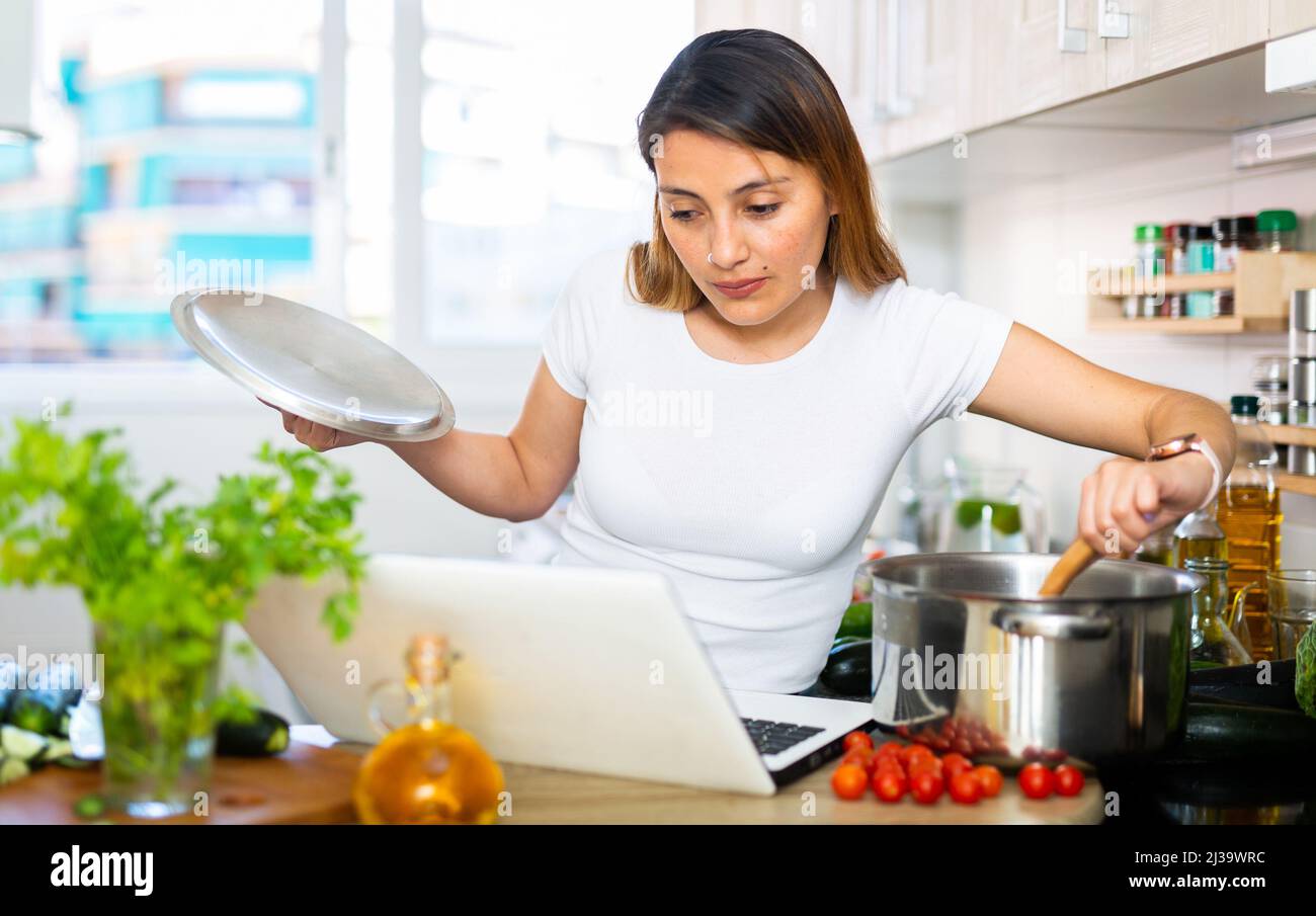 Woman cooking soup and watching movie at laptop Stock Photo - Alamy