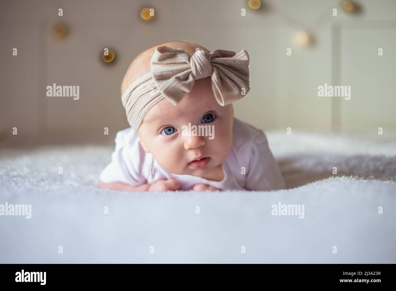 Baby girl 3 months old lies on a bed with white clothes on her stomach ...
