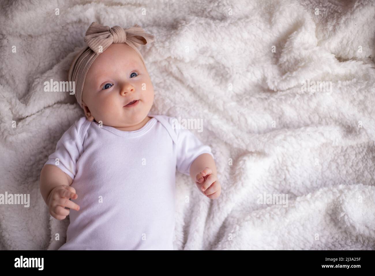 baby girl lying on a white blanket in white clothes on her stomach and ...