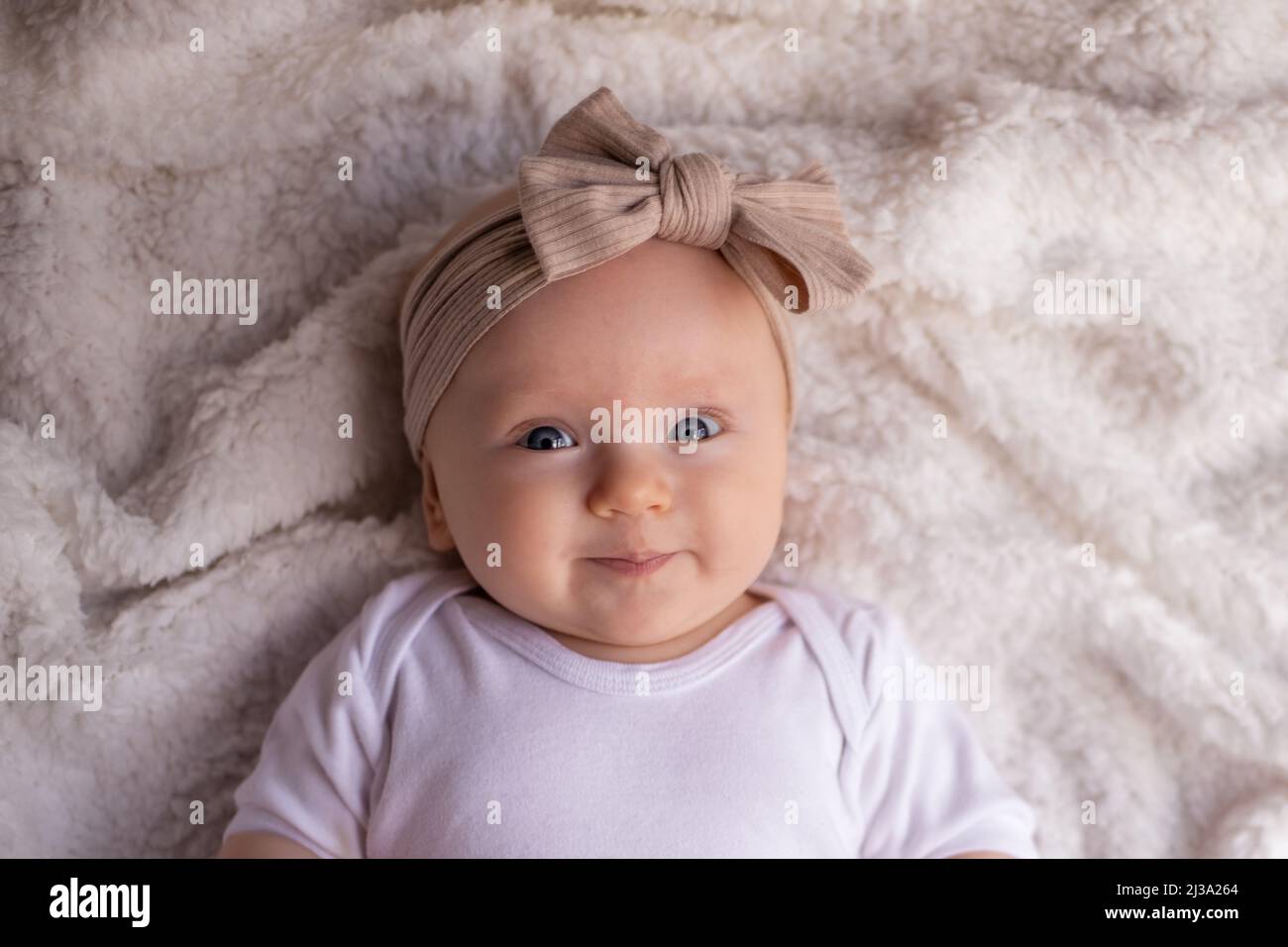 baby girl lying on a white blanket in white clothes on her stomach and ...