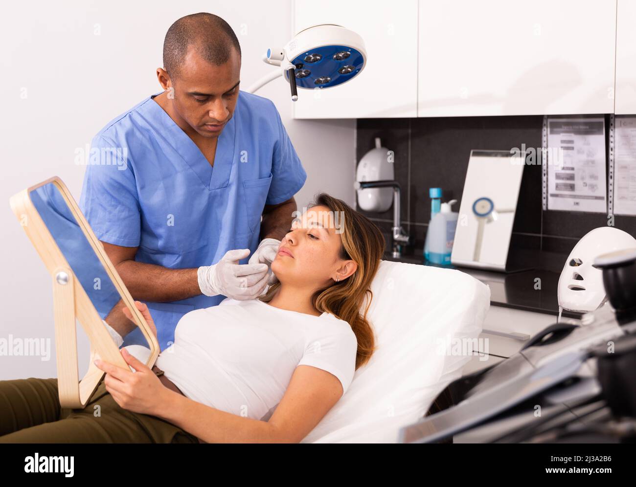 Cosmetologist examining female client face before procedure Stock Photo ...