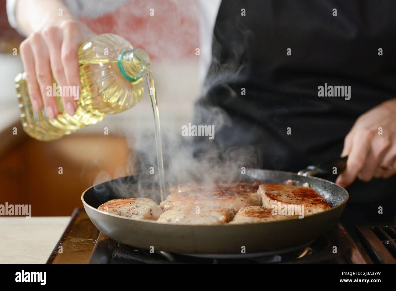 The chef in the kitchen prepares fresh pork steaks on a griddle with ...