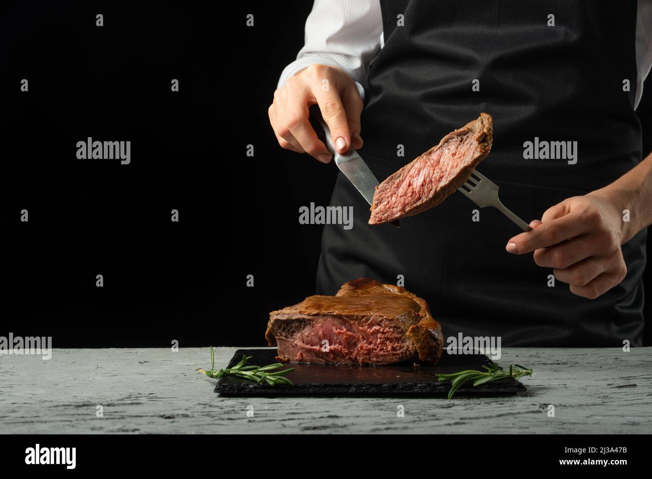 Chef, cut with a meat steak on a black background with an open space ...