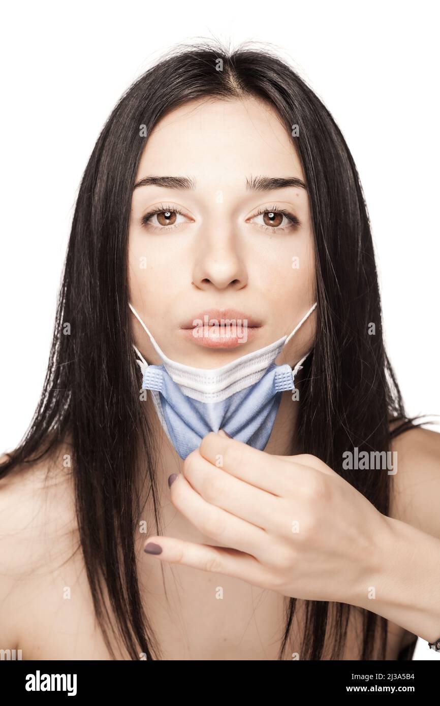 Serious looking girl pulling away medical face mask. Portrait against ...