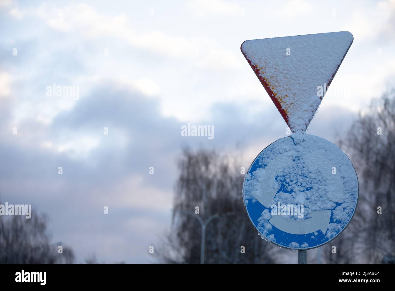 Snowy road sign, intersection with circular traffic Stock Photo - Alamy