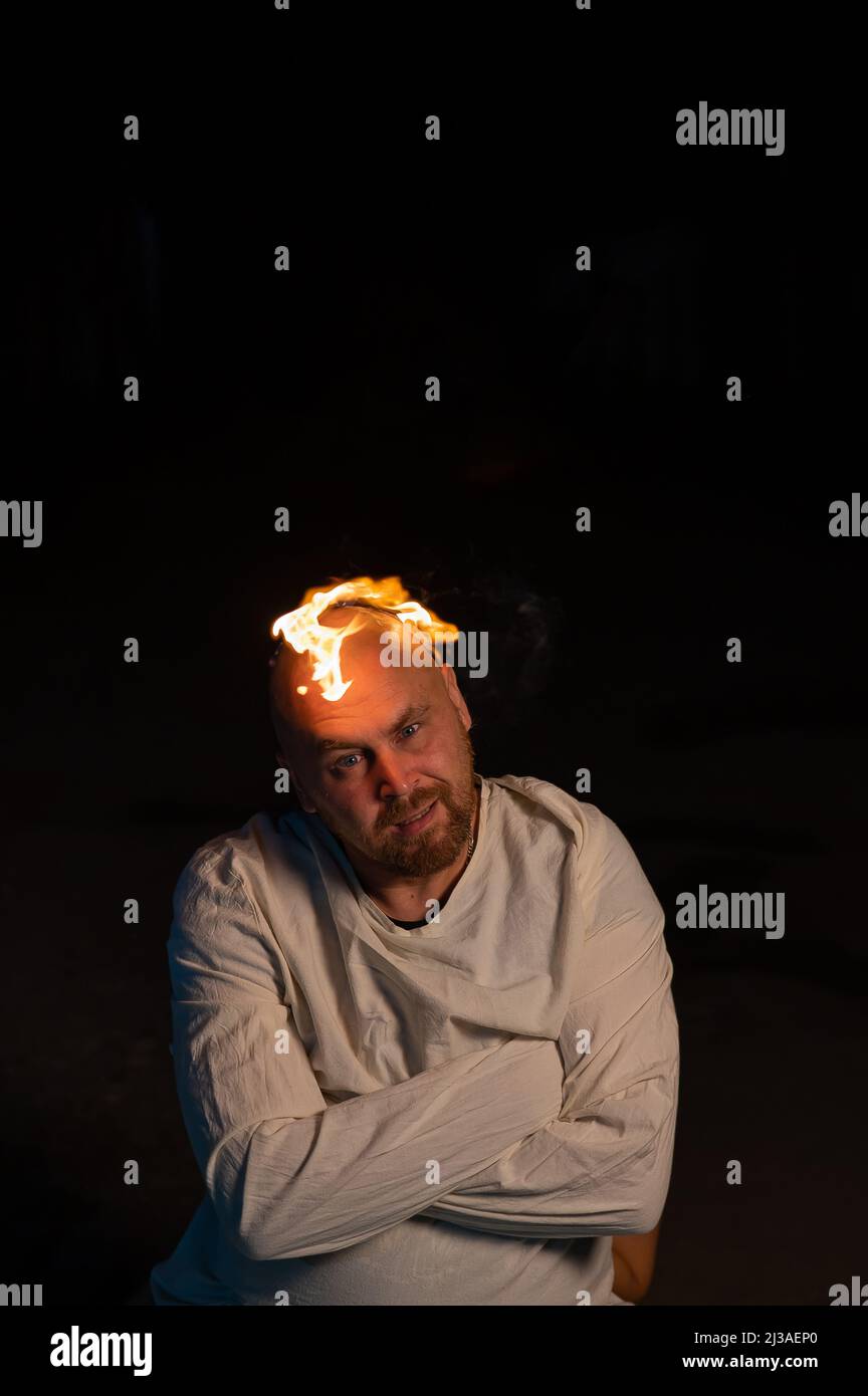 Bald man in a straitjacket with a burning head on a dark background ...