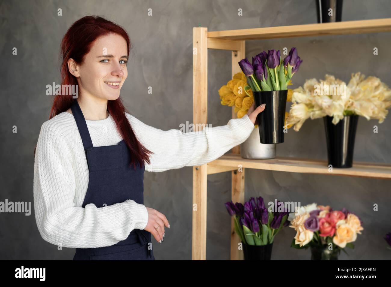 Small business. woman florist in flower shop near showcase with tulips ...