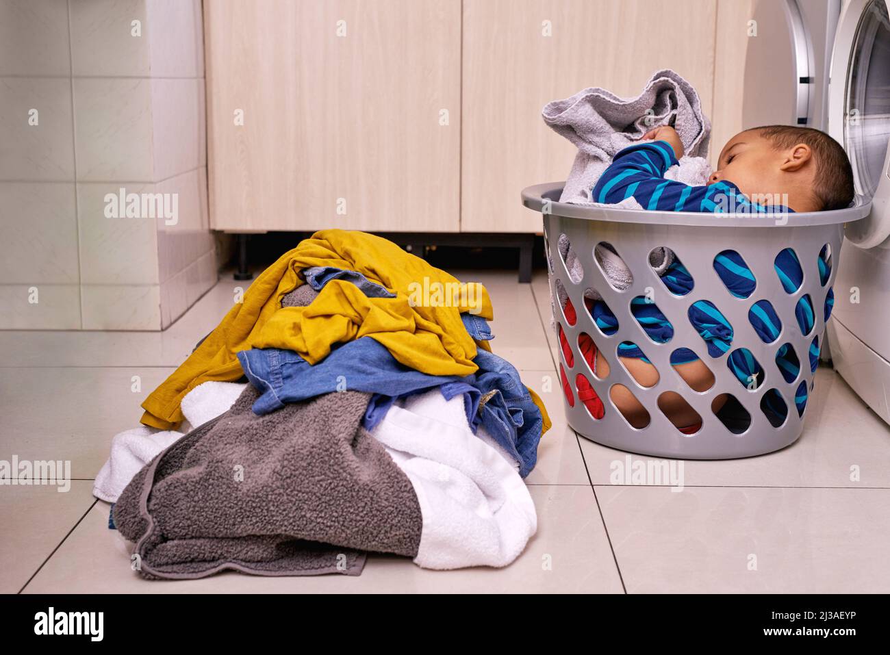 Taking a quick snooze. Shot of a little boy sleeping in a laundry ...