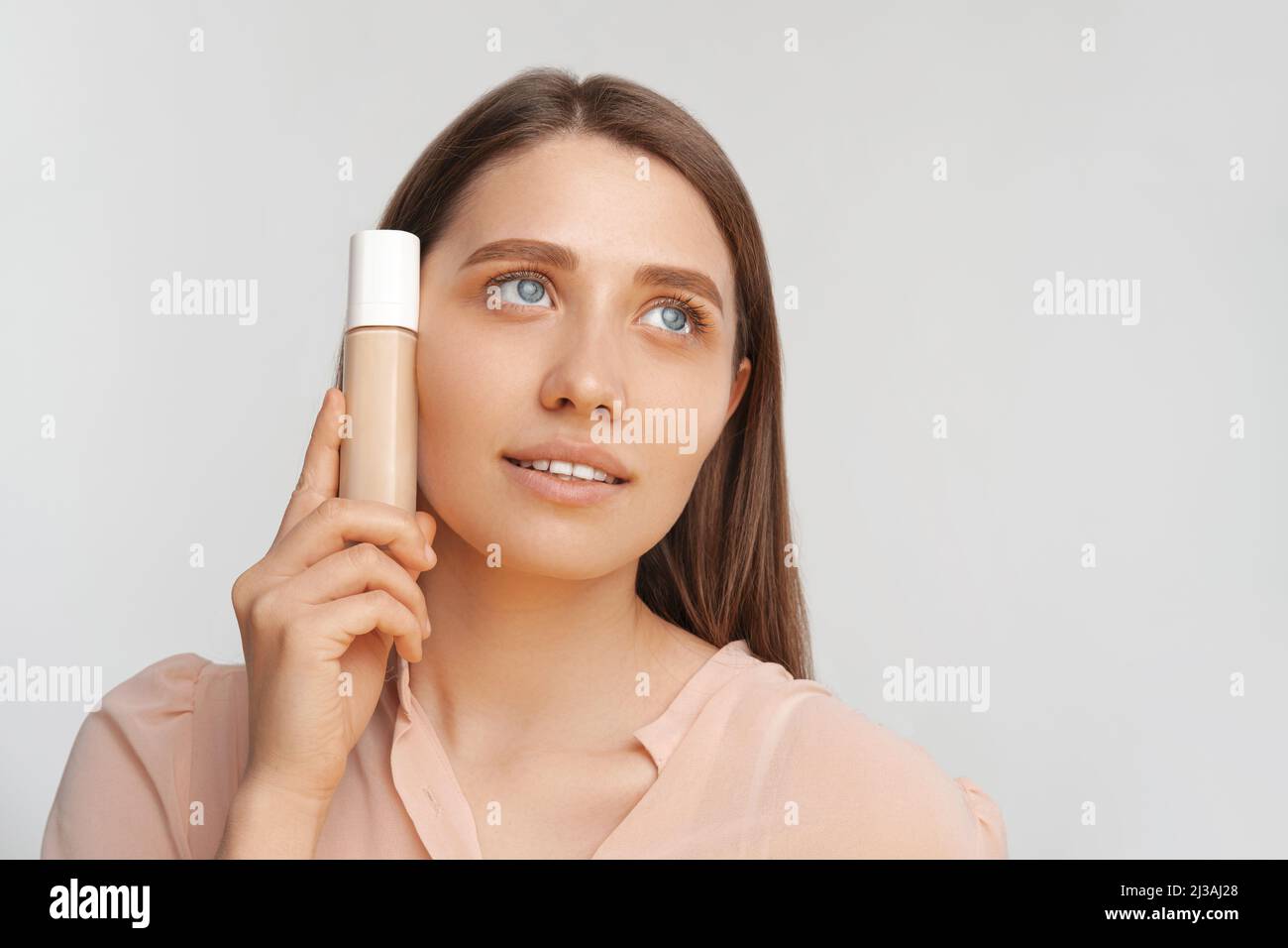 Fresh young smiling woman is holding a foundation cream tube near her ...