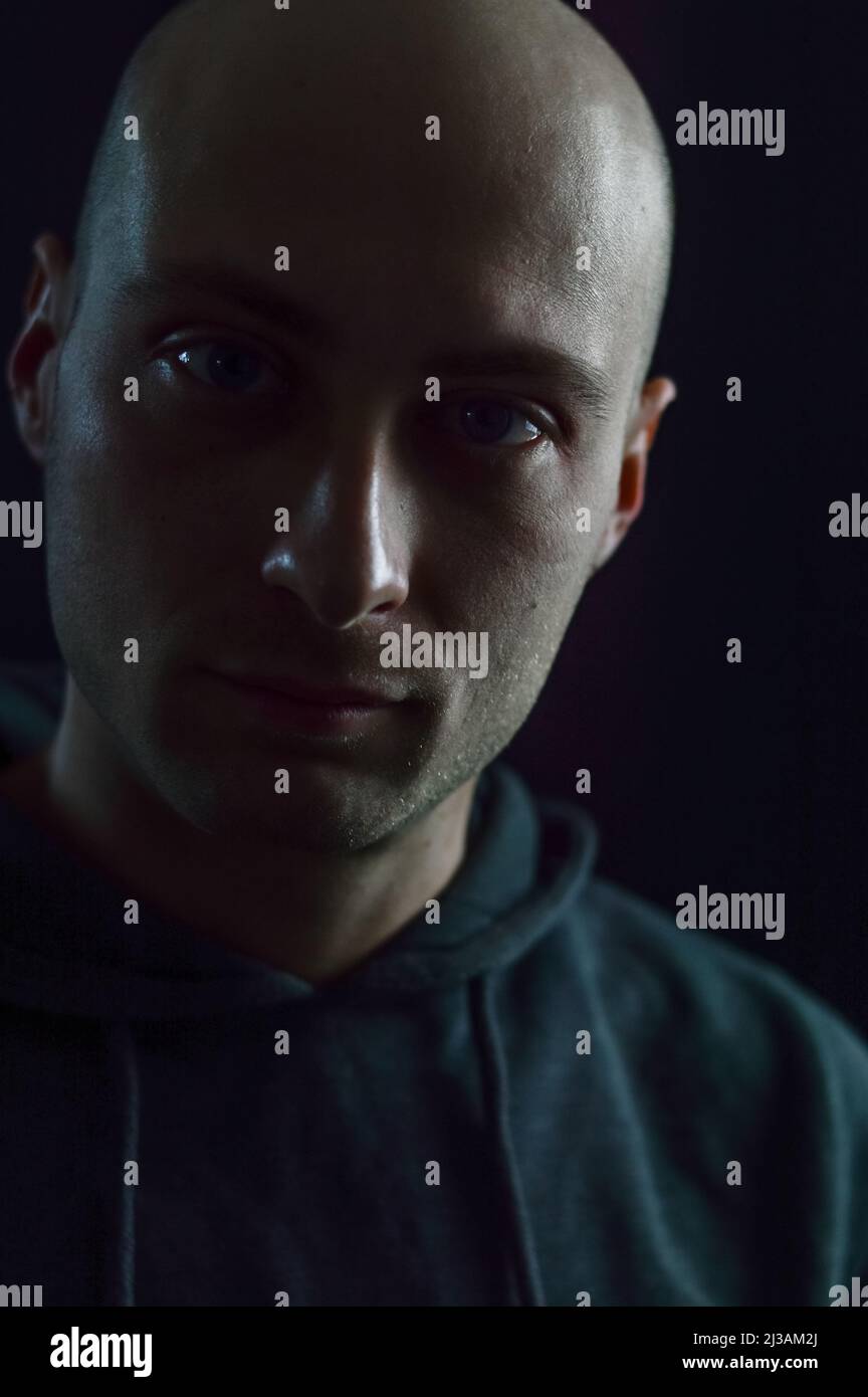Portrait of a young bald man in the dark with a serious and scary look ...