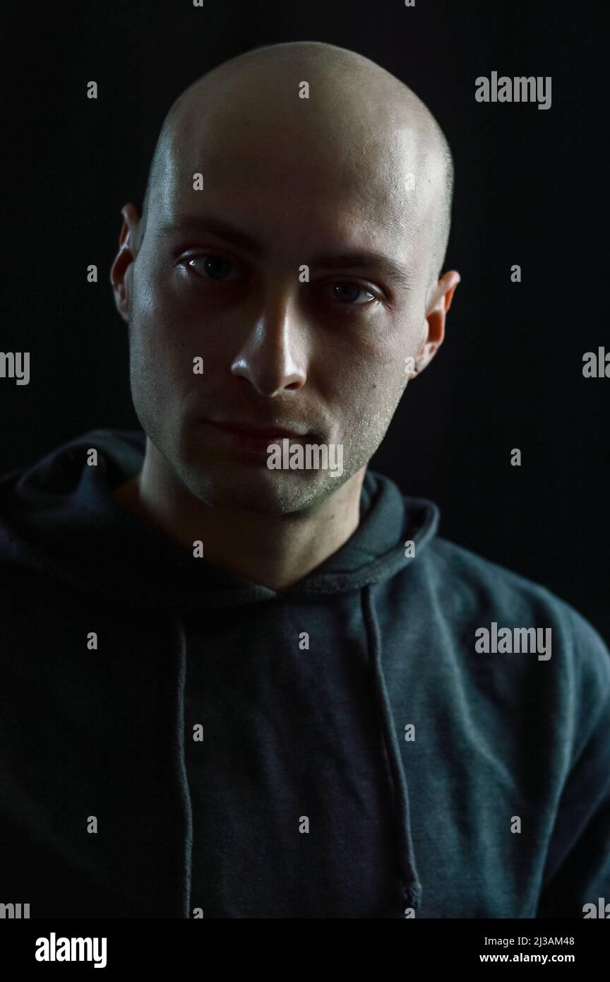 Portrait of a young bald man in the dark with a serious and scary look ...