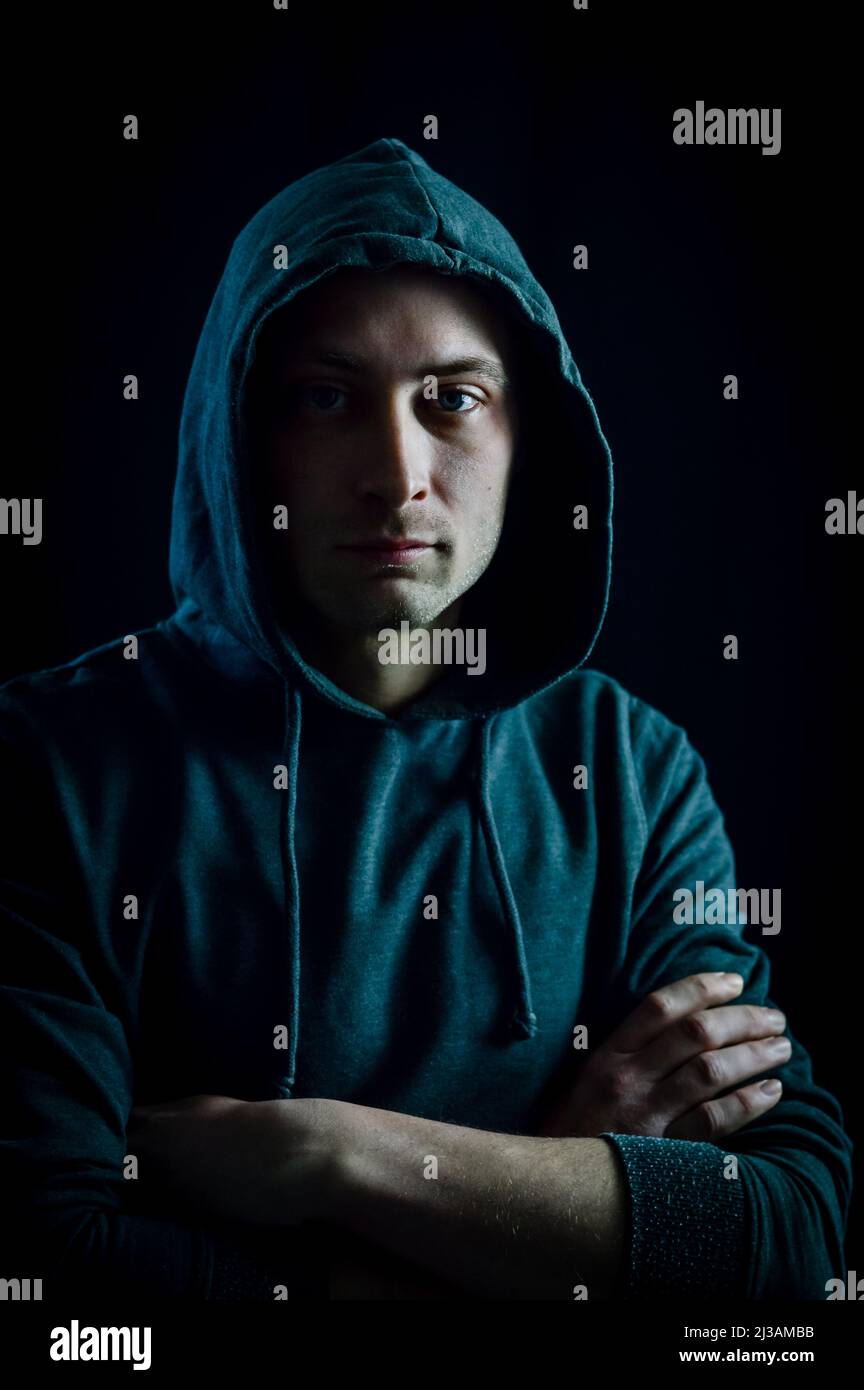 Portrait of a handsome young blue-eyed hooded man with his arms crossed ...