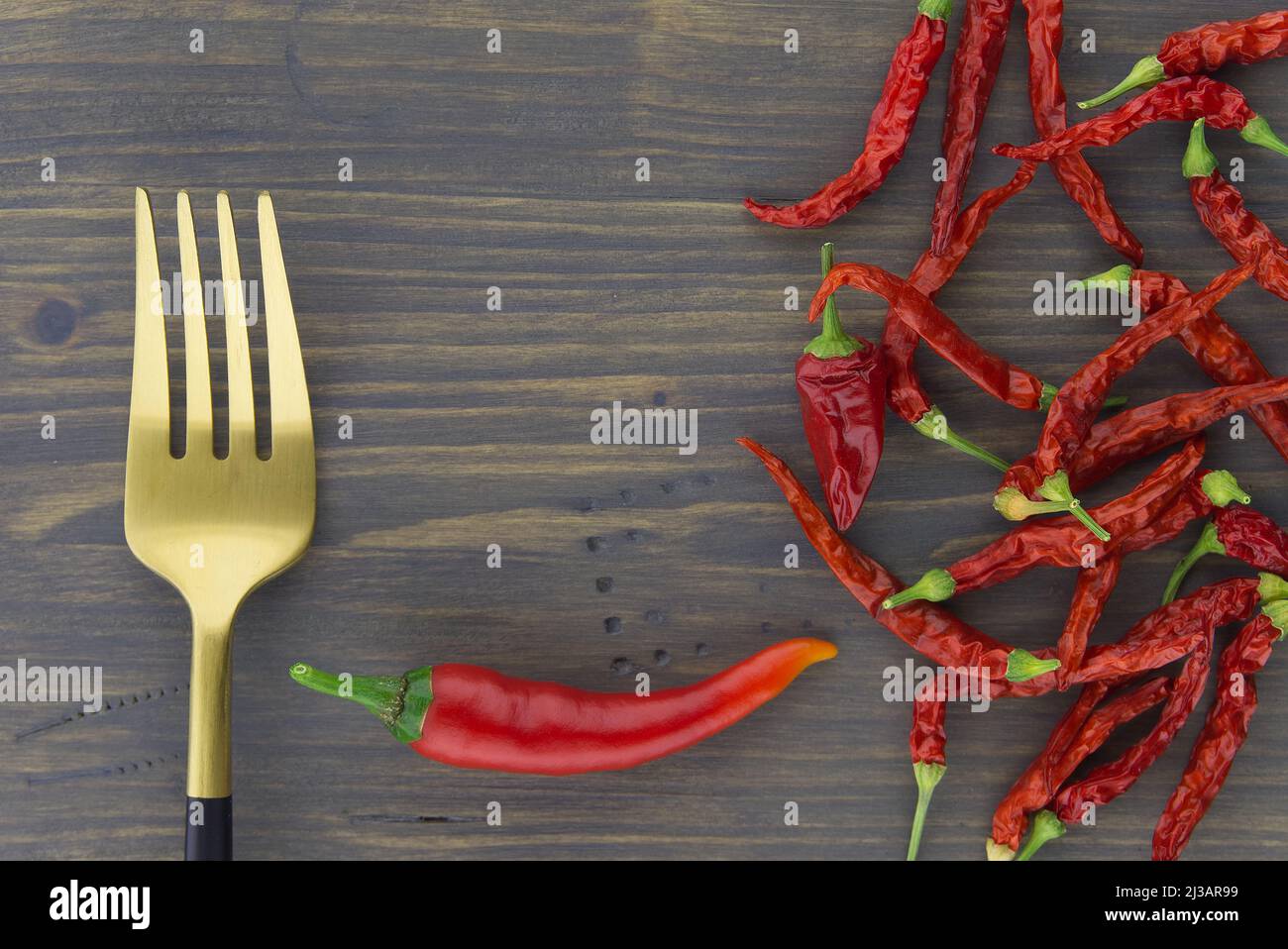 Fresh and dried red chillies with golden cutlery over a wood background ...