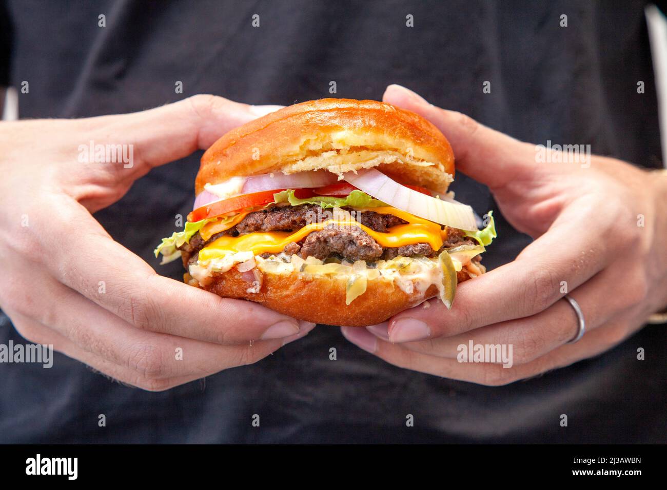 Hands holding a doughnut bun double beef patty burger with veggies ...