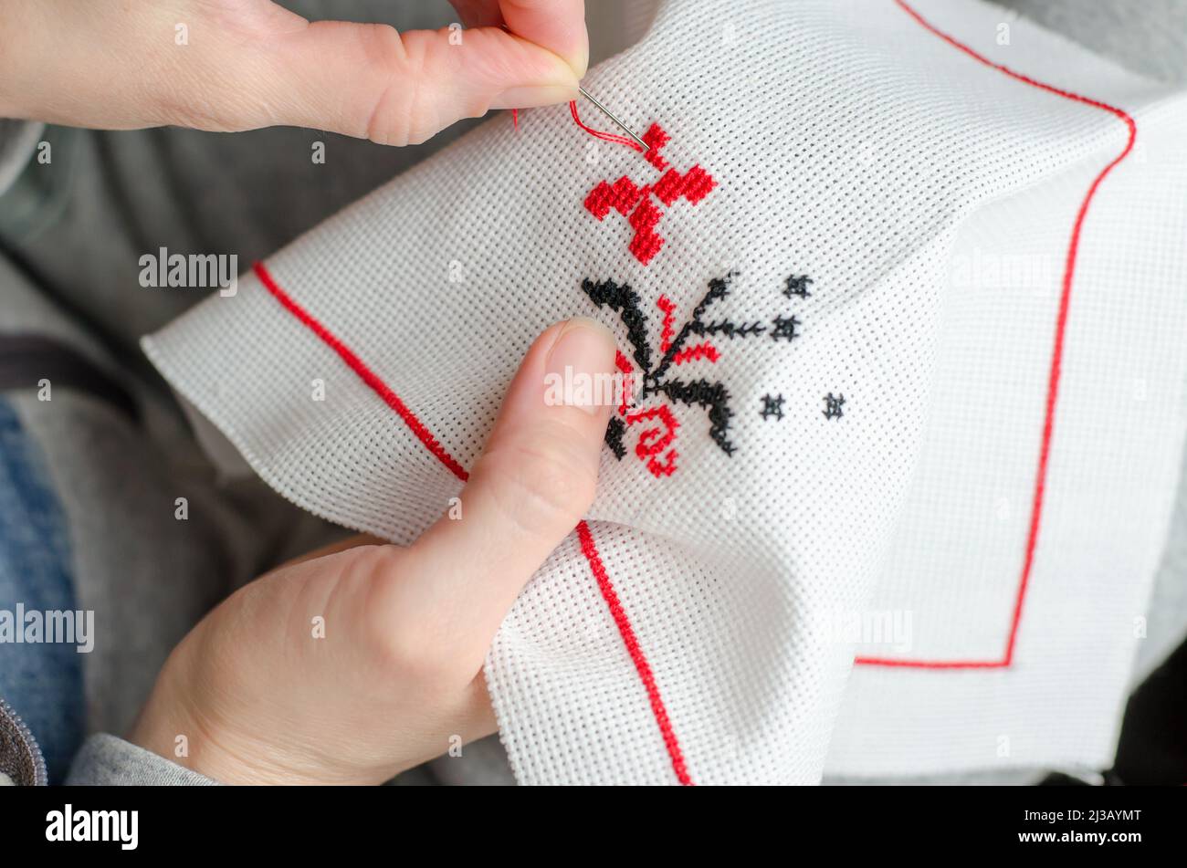 Close-up of female hands embroider with a cross on a white canvas. A ...