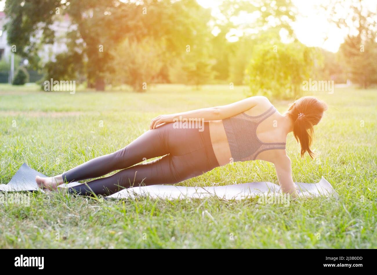 Young sportive woman performs exercises in nature. Woman practices yoga ...