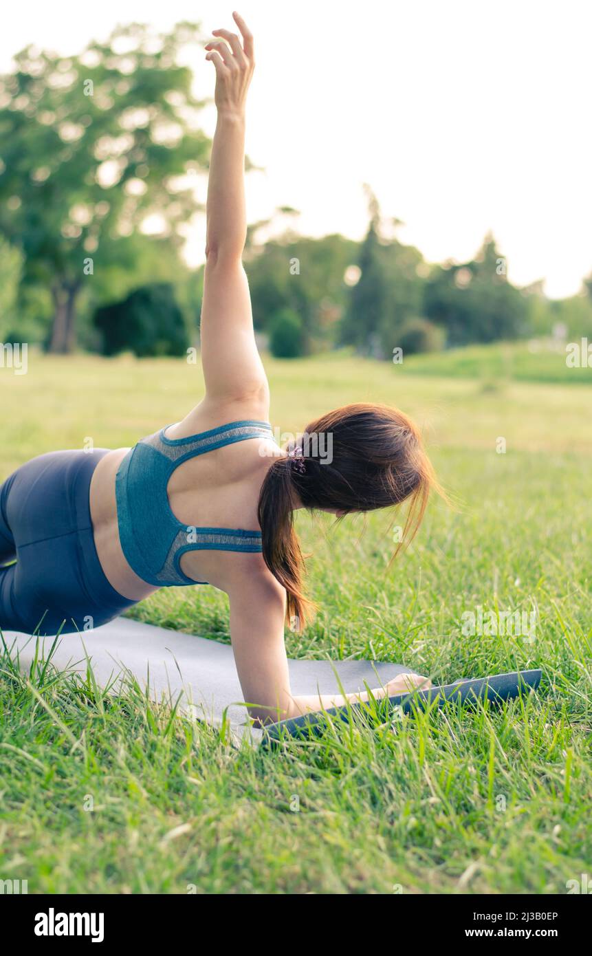 Young woman performs exercises in the park on the mat. The woman goes ...