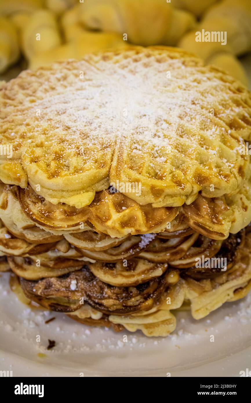 A stack of baked waffles with powdered sugar topping on a buffet table ...