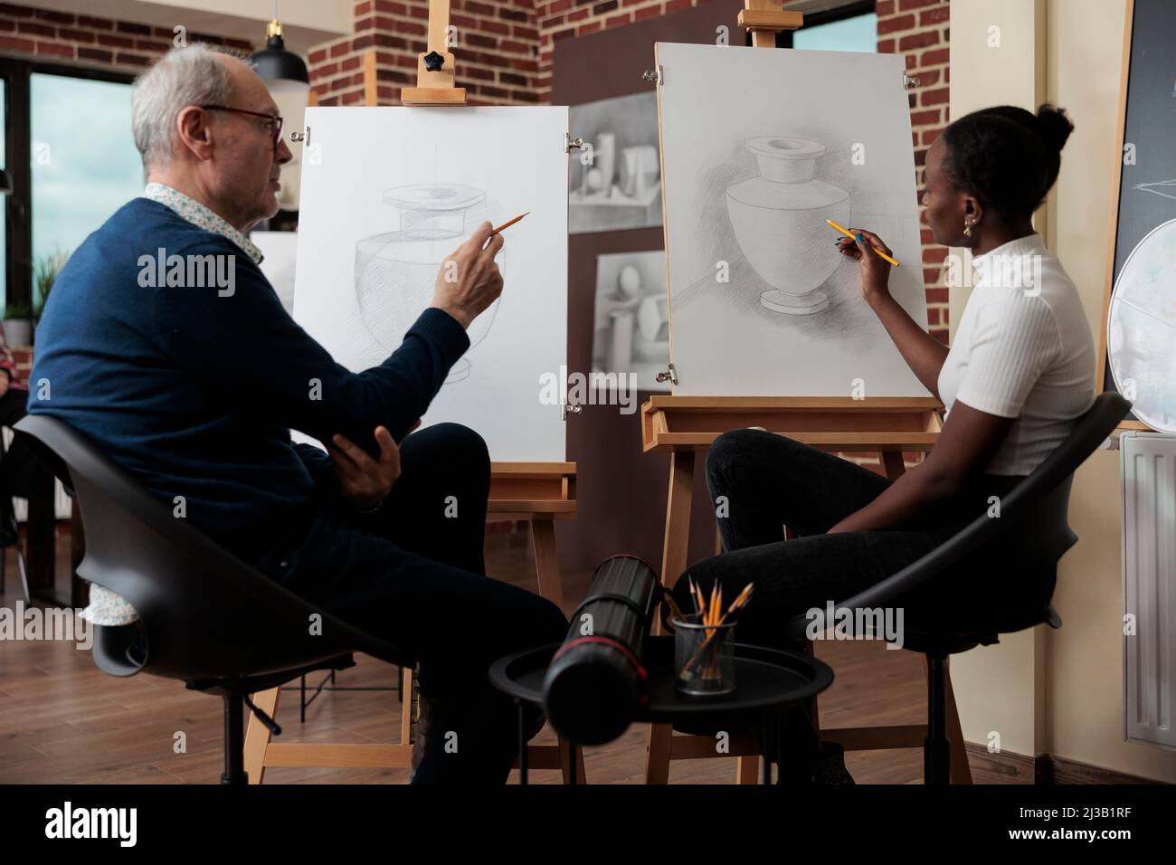 Senior painter teacher explaining sketching lesson to young student ...