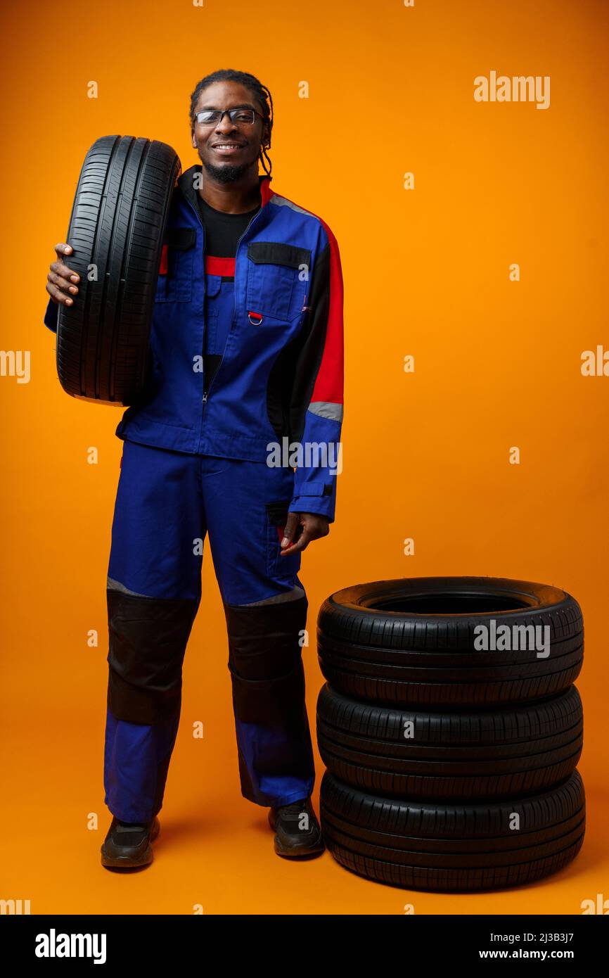 African american car service worker with car tyre against yellow ...