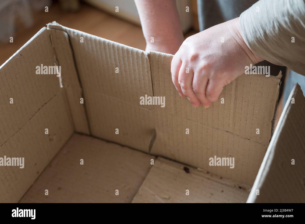 An adult woman cuts through a cardboard box with a knife. The woman's ...
