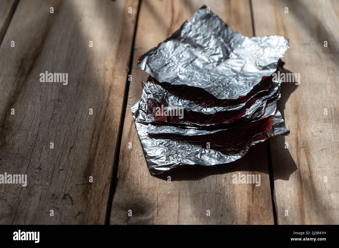 A stack of rectangular aluminum candy wrappers against a wooden ...
