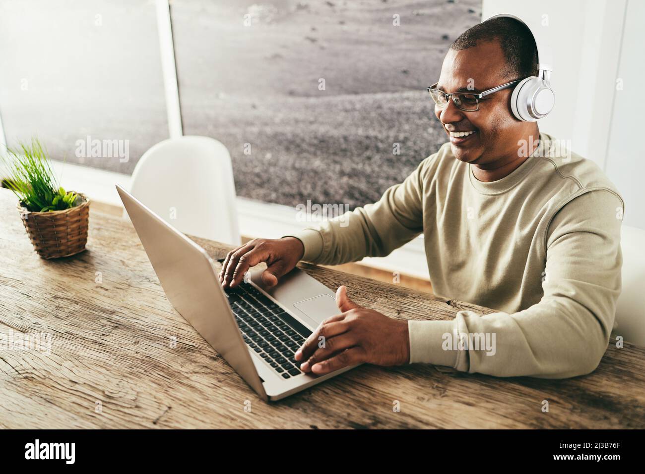 Senior african man using laptop computer while wearing headphones at ...