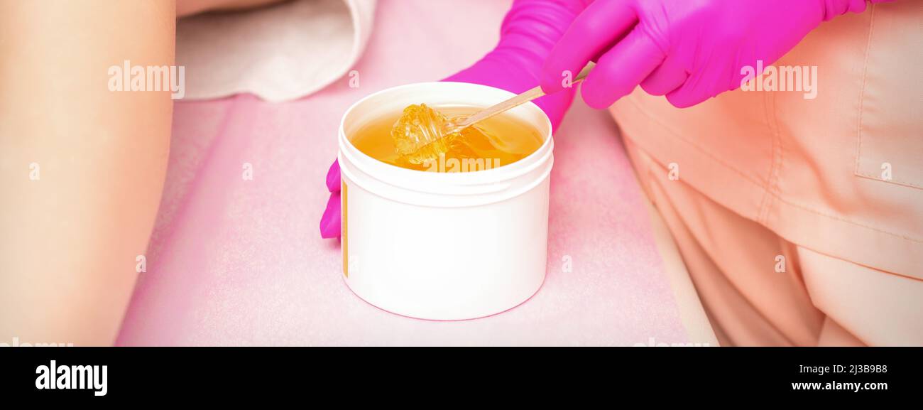 Beautician with a white jar of wax sugaring before hair removal at the ...
