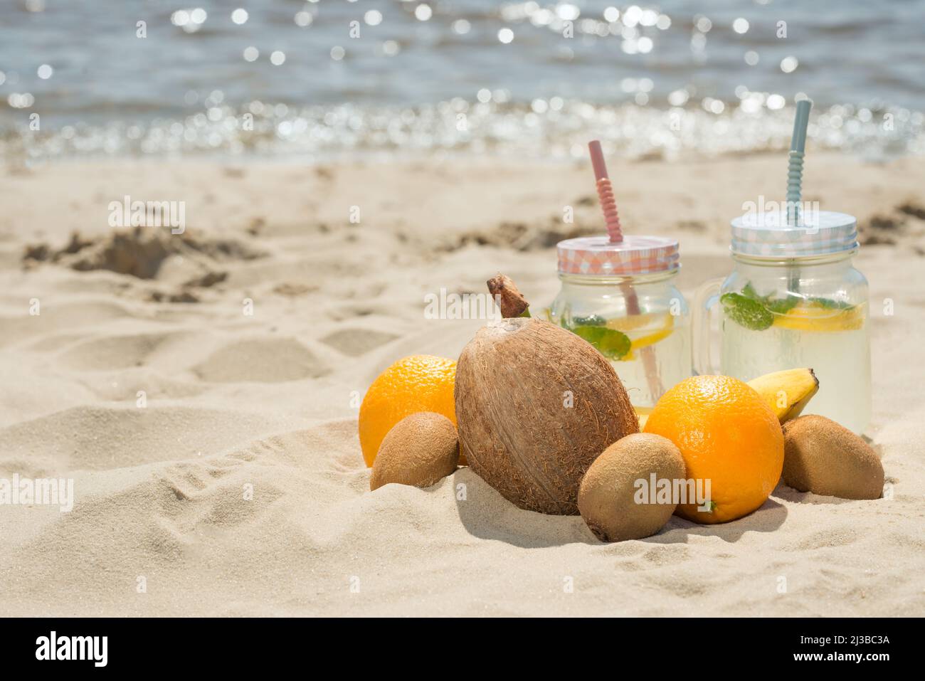 Tropical fruits and mojito on white sand on the beach of the sea or ...