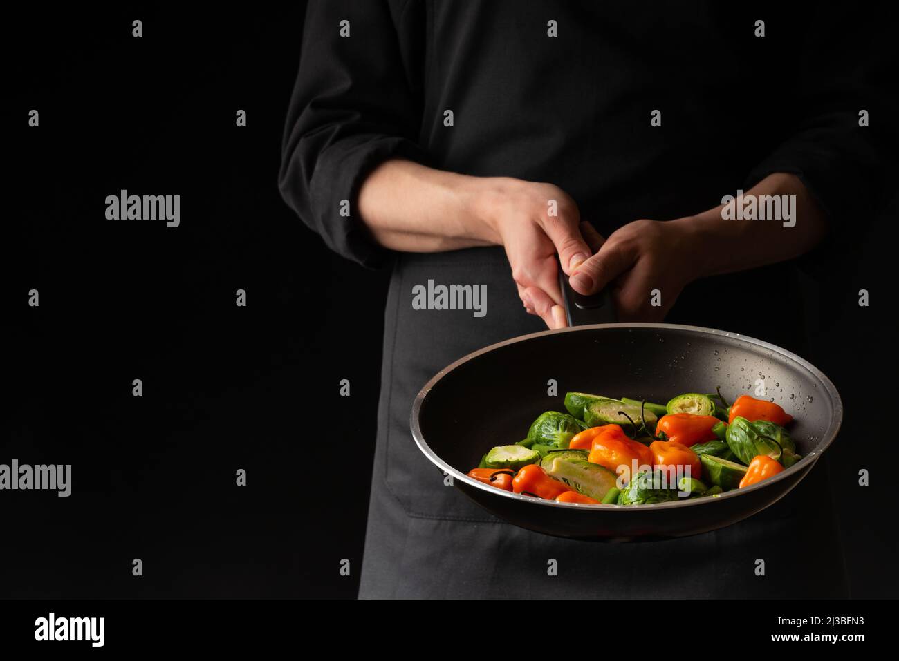 Chef preparing vegetables in a pan, Asian cuisine, on a black ...
