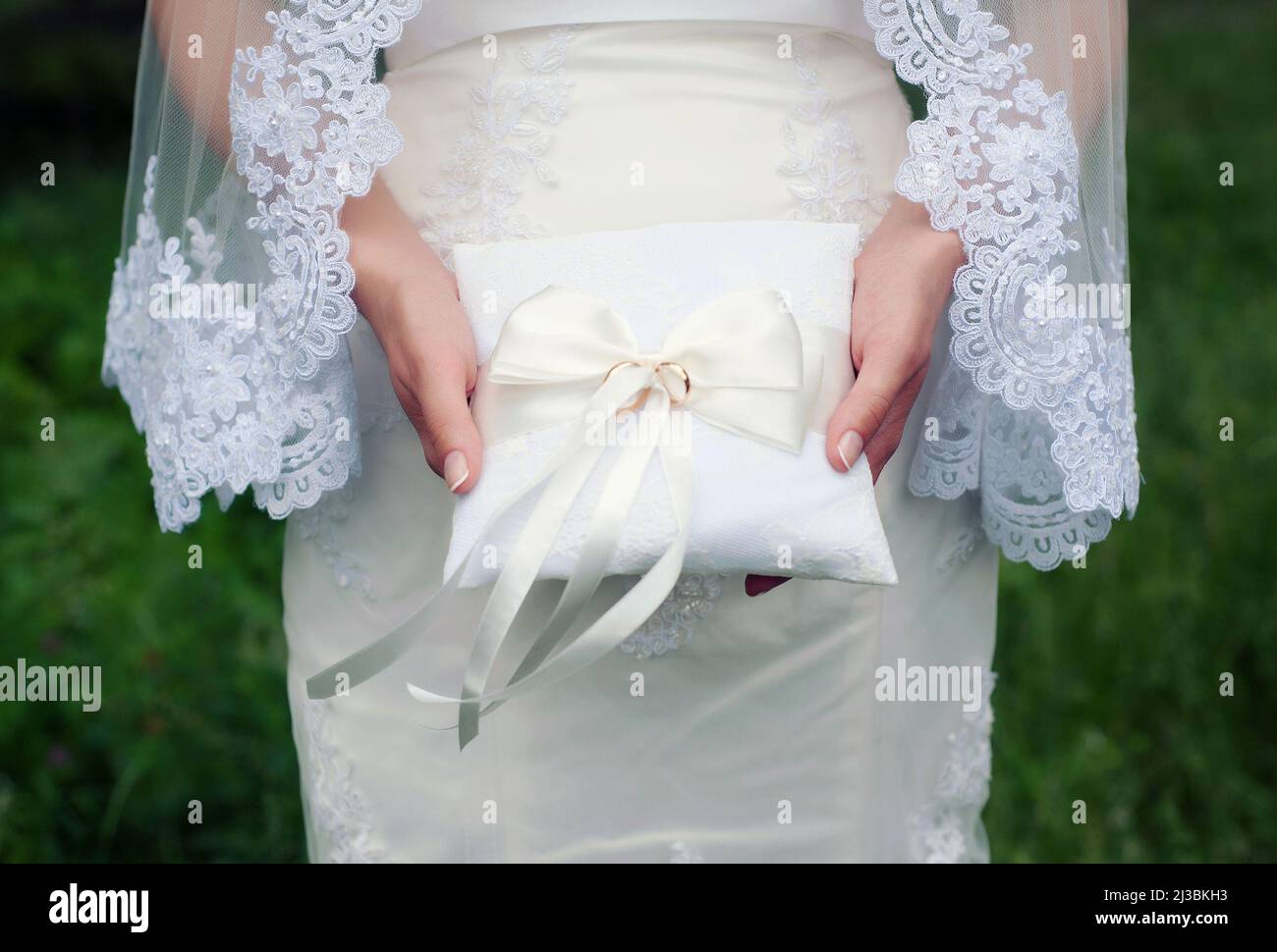 Wedding rings on white pillow in the hands of the bride. Bride in a ...