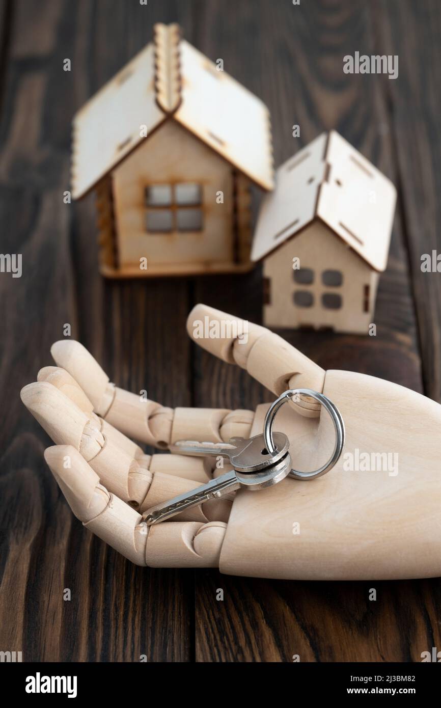 Wooden doll's hand with keys on its palm with toy wooden houses on a ...
