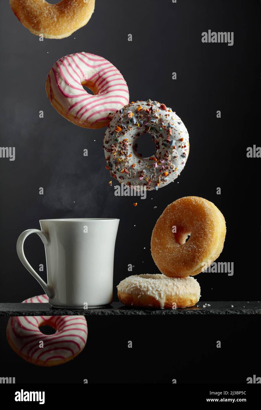 Sweet tasty donuts and a white mug with hot drink on a black background ...