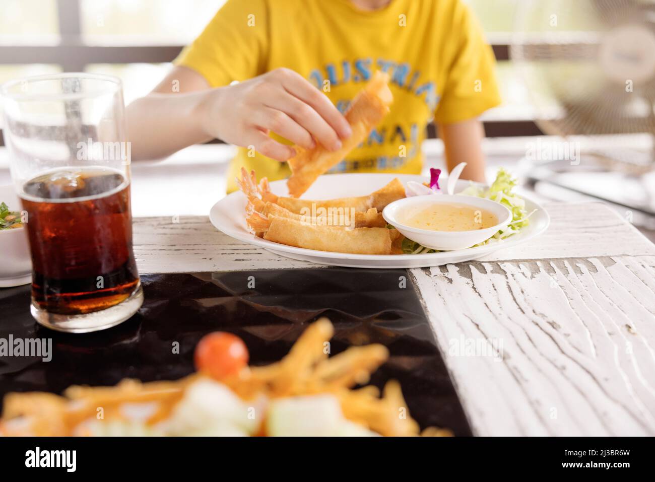 Boy sitting at table and eating spring rolls Stock Photo - Alamy