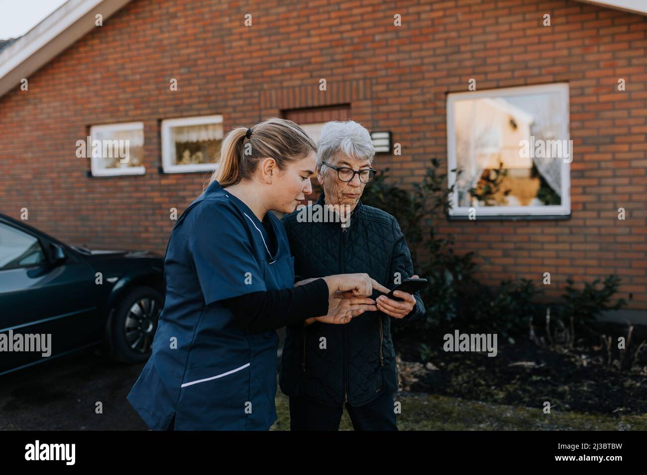 Home caretaker helping senior woman use phone Stock Photo - Alamy